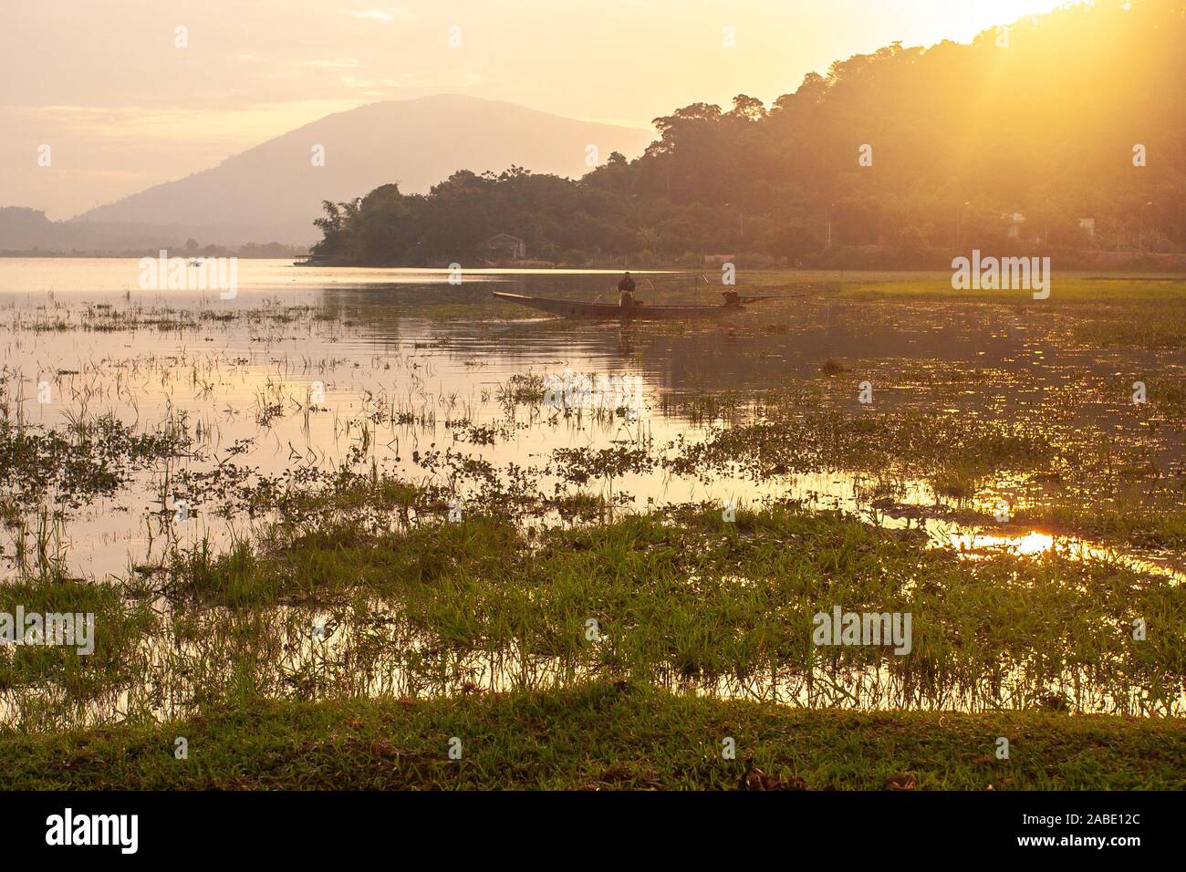 Sunny dawn on the lake with a boat and a fisherman. The boat is Asian ...