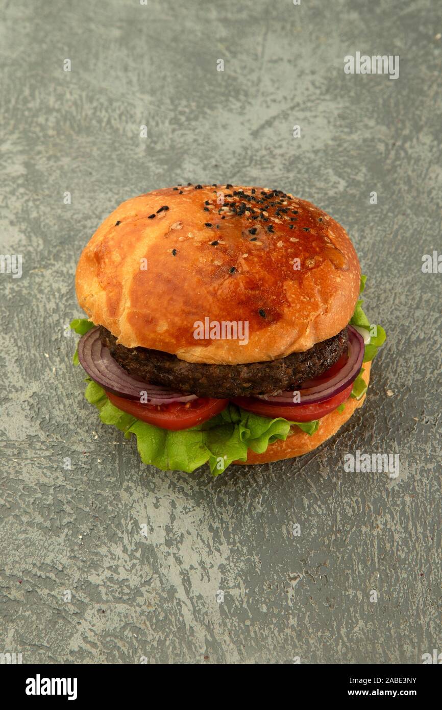 top view of beef burger with lettuce, tomato, onion in plain grey ...