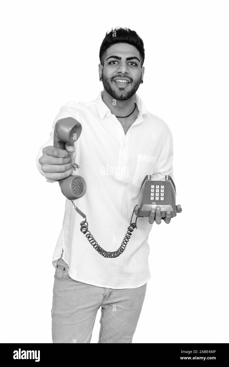 Studio shot of young happy Indian man giving telephone isolated against ...