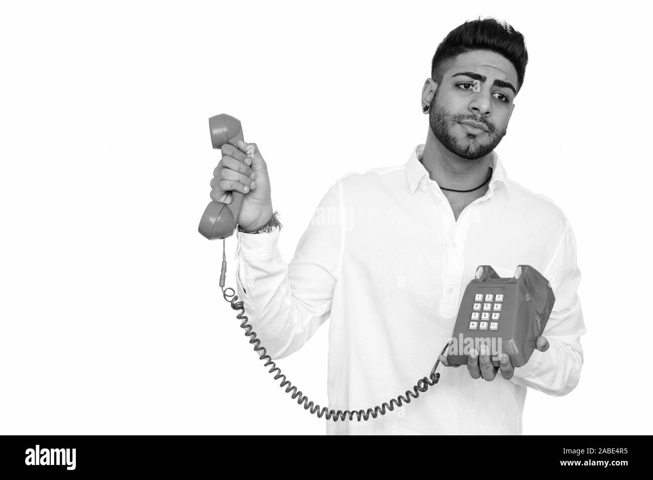 Studio shot of young handsome Indian man looking annoyed while holding ...