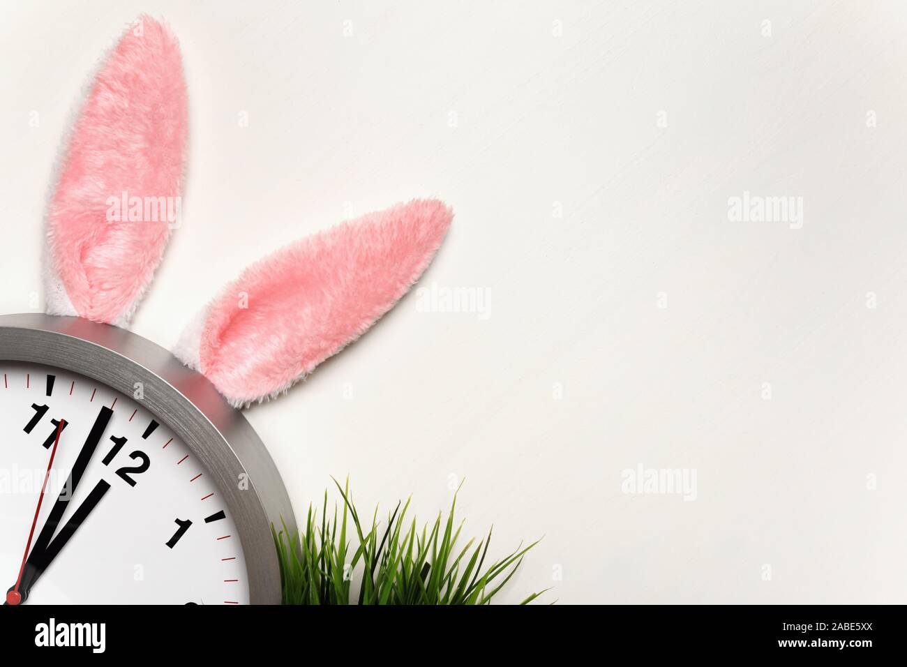 Easter concept. Clock with bunny ears and green grass on a white ...