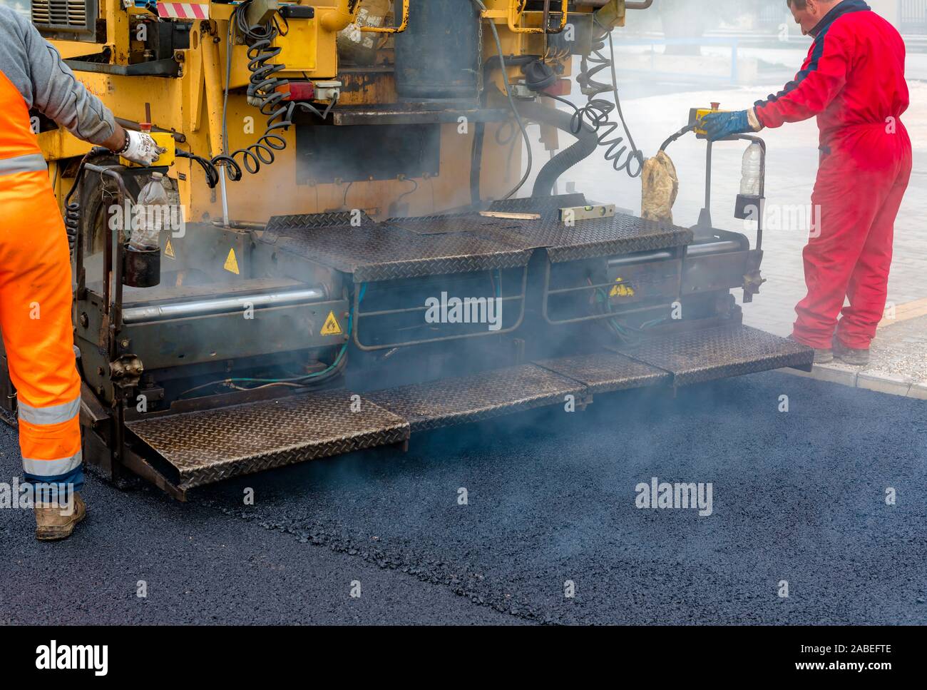 Workers regulate tracked paver laying asphalt heated to temperatures ...