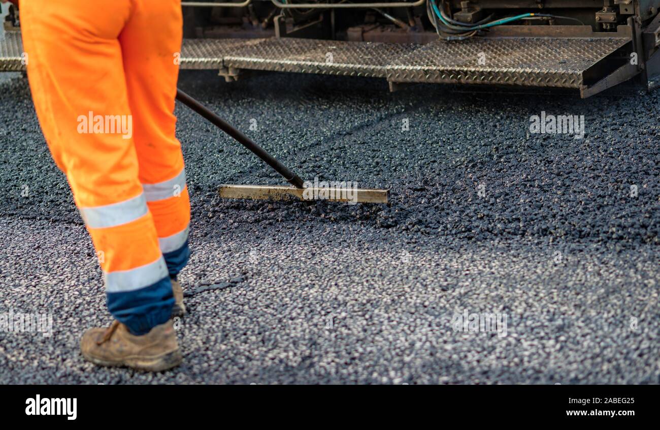 Workers regulate tracked paver laying asphalt heated to temperatures ...