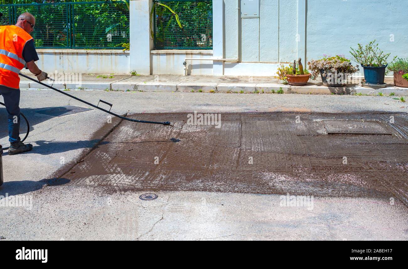 Road worker spraying bitumen emulsion with the hand spray lance before ...