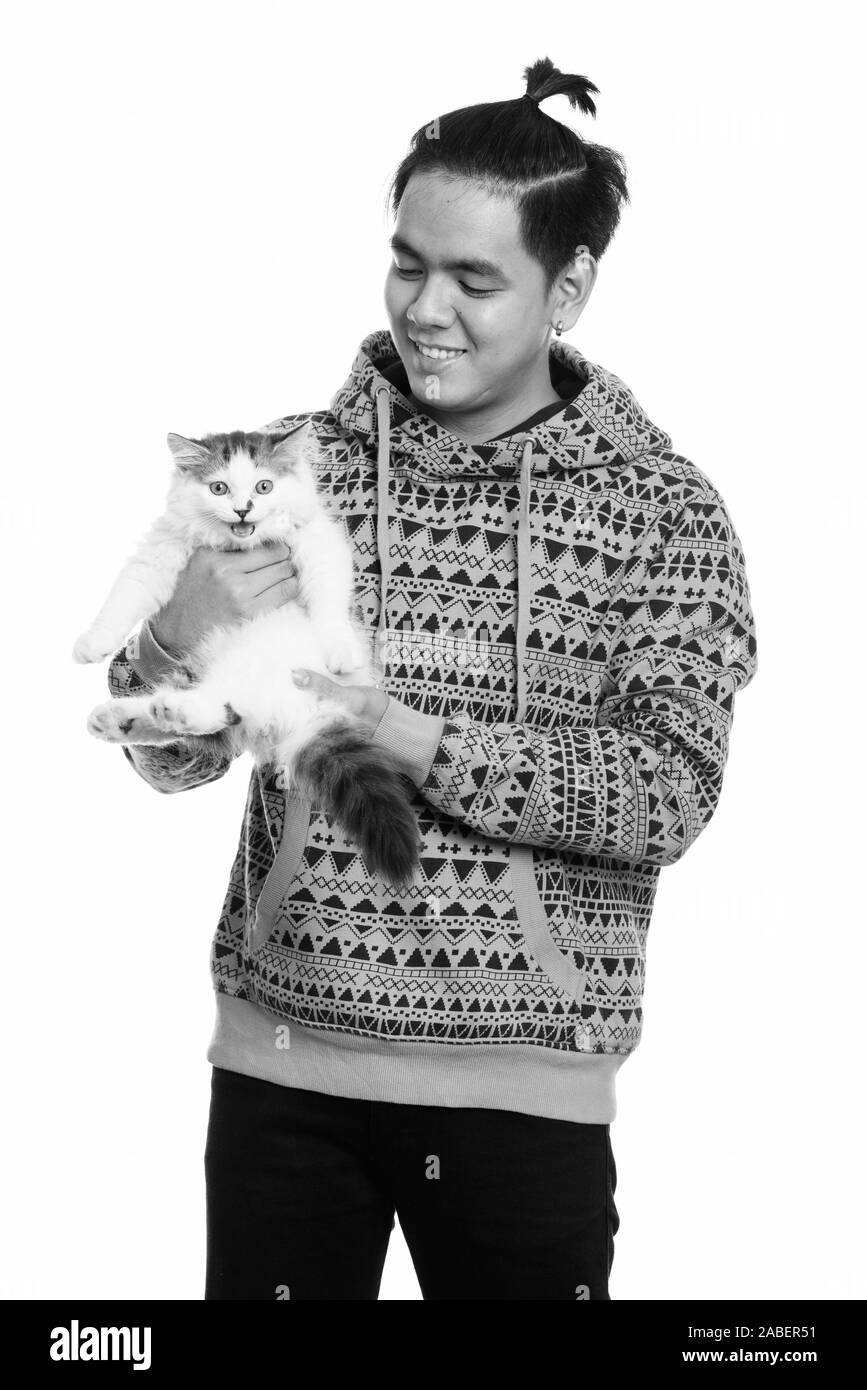 Studio shot of young happy Asian man smiling while holding cute cat ...
