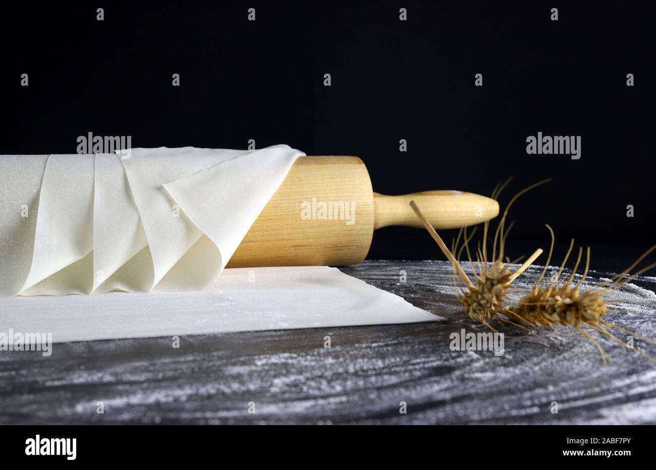 Closeup of phyllo dough on a floured table. Dark background with ...