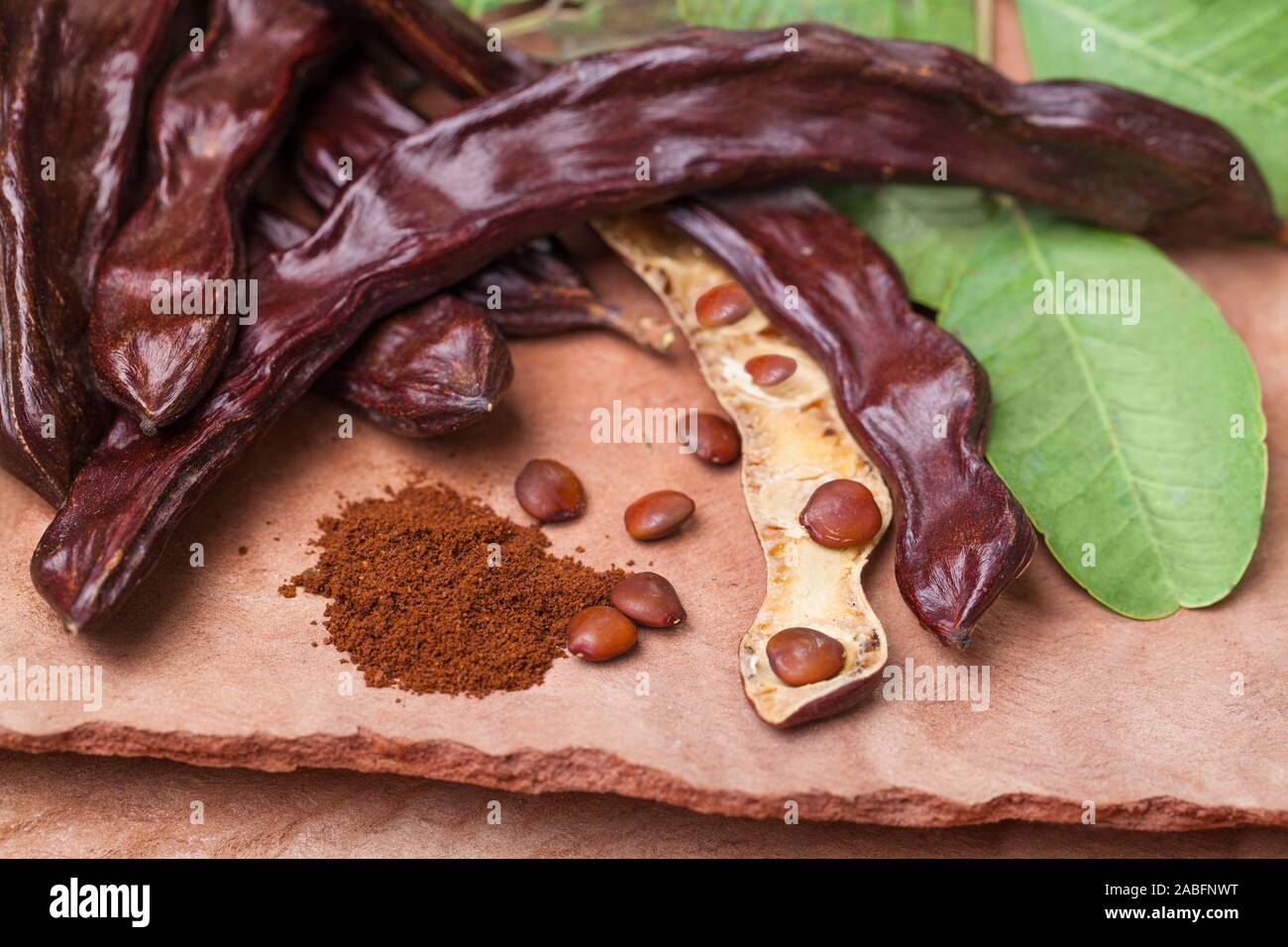 Carob. Organic carob pods with seeds and leaves on tree bark table ...