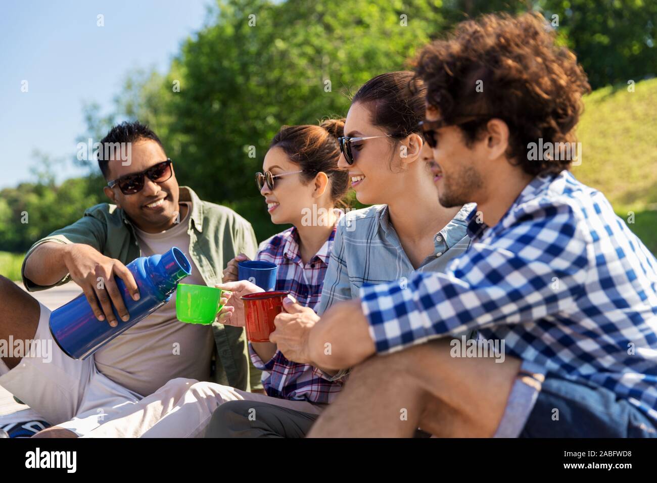happy friends drinking tea from thermos in summer Stock Photo - Alamy