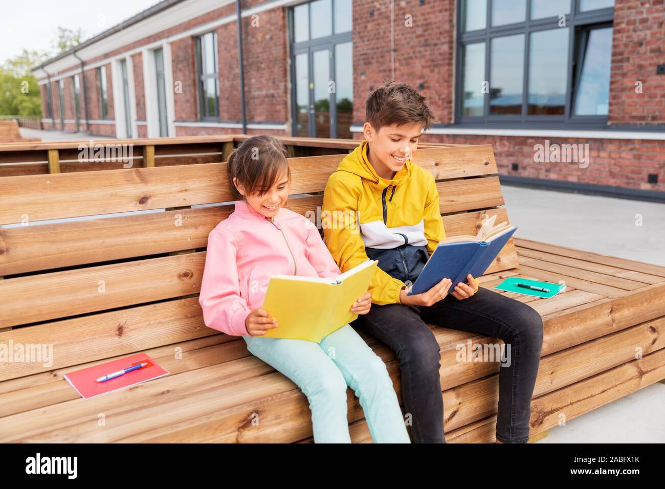 school children reading books sitting on bench Stock Photo - Alamy