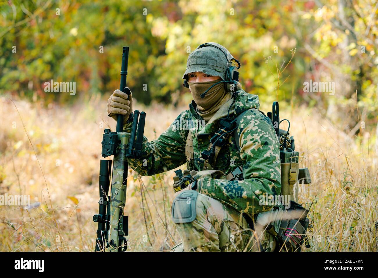 Airsoft man in uniform with sniper rifle, lurking in grass on forest ...