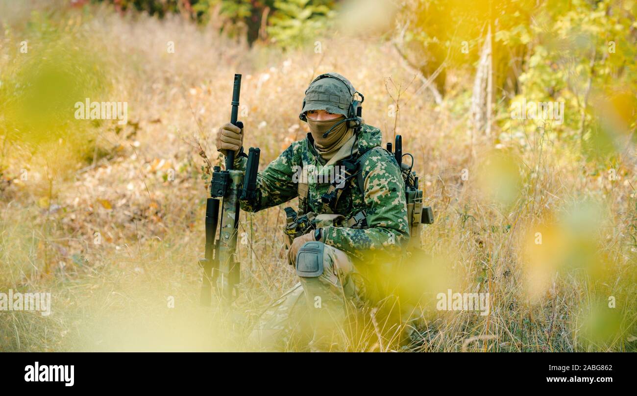 Airsoft man in uniform with sniper rifle, lurking in grass on forest ...