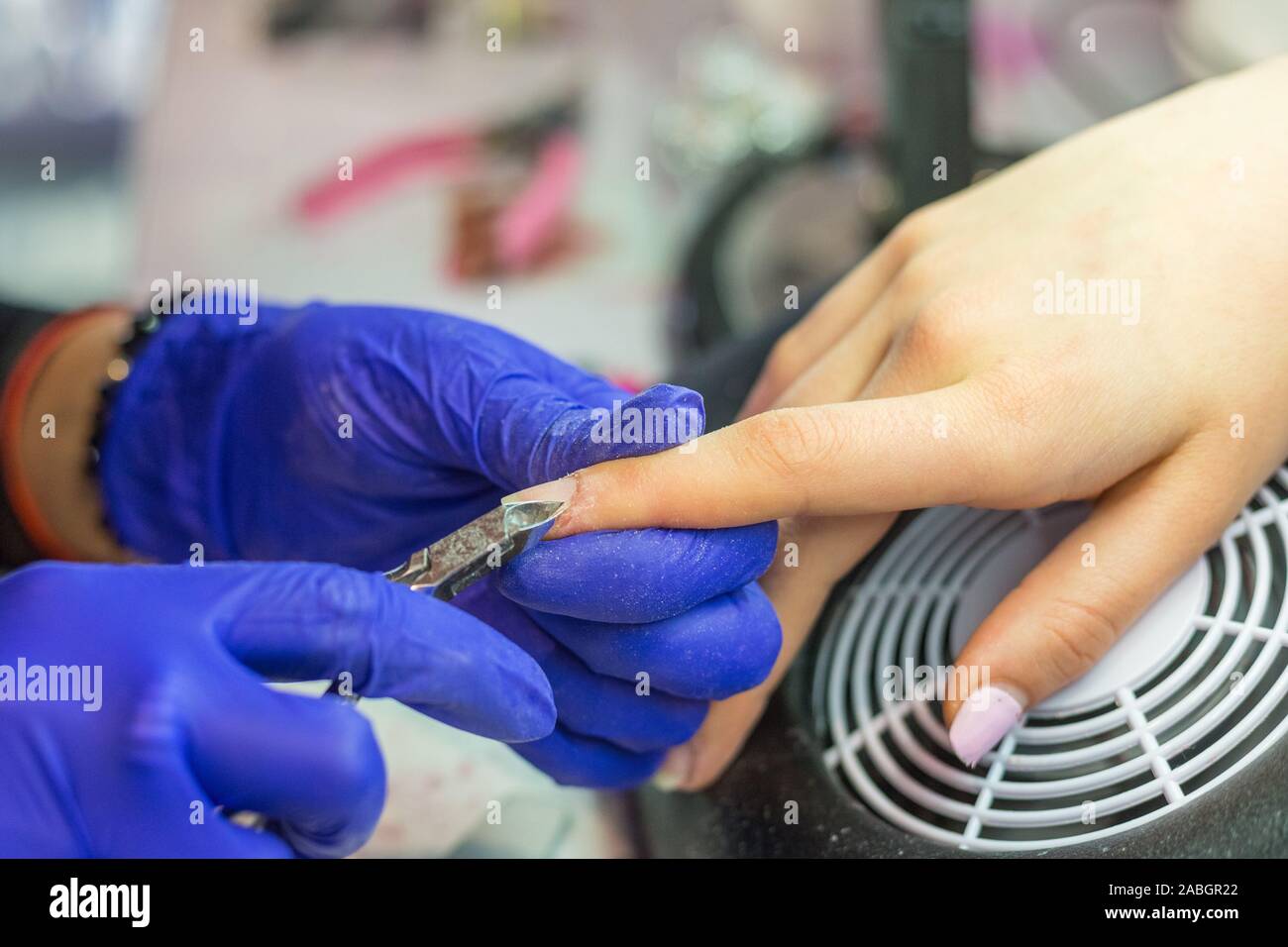 Manicurist with blue gloves rasping nails on women's hand in nail salon ...