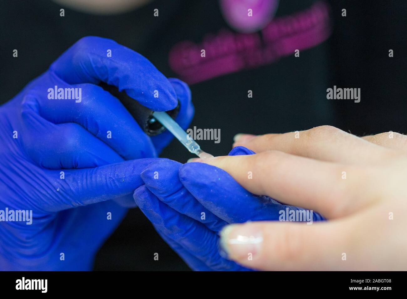 Manicurist with blue gloves polish nails on women's hand in nail salon ...