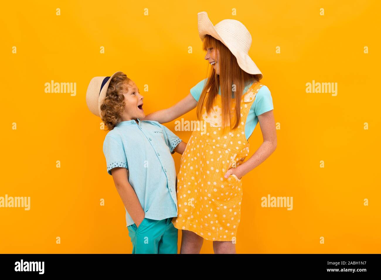Two red-haired friends in summer hats look at each other on a yellow ...