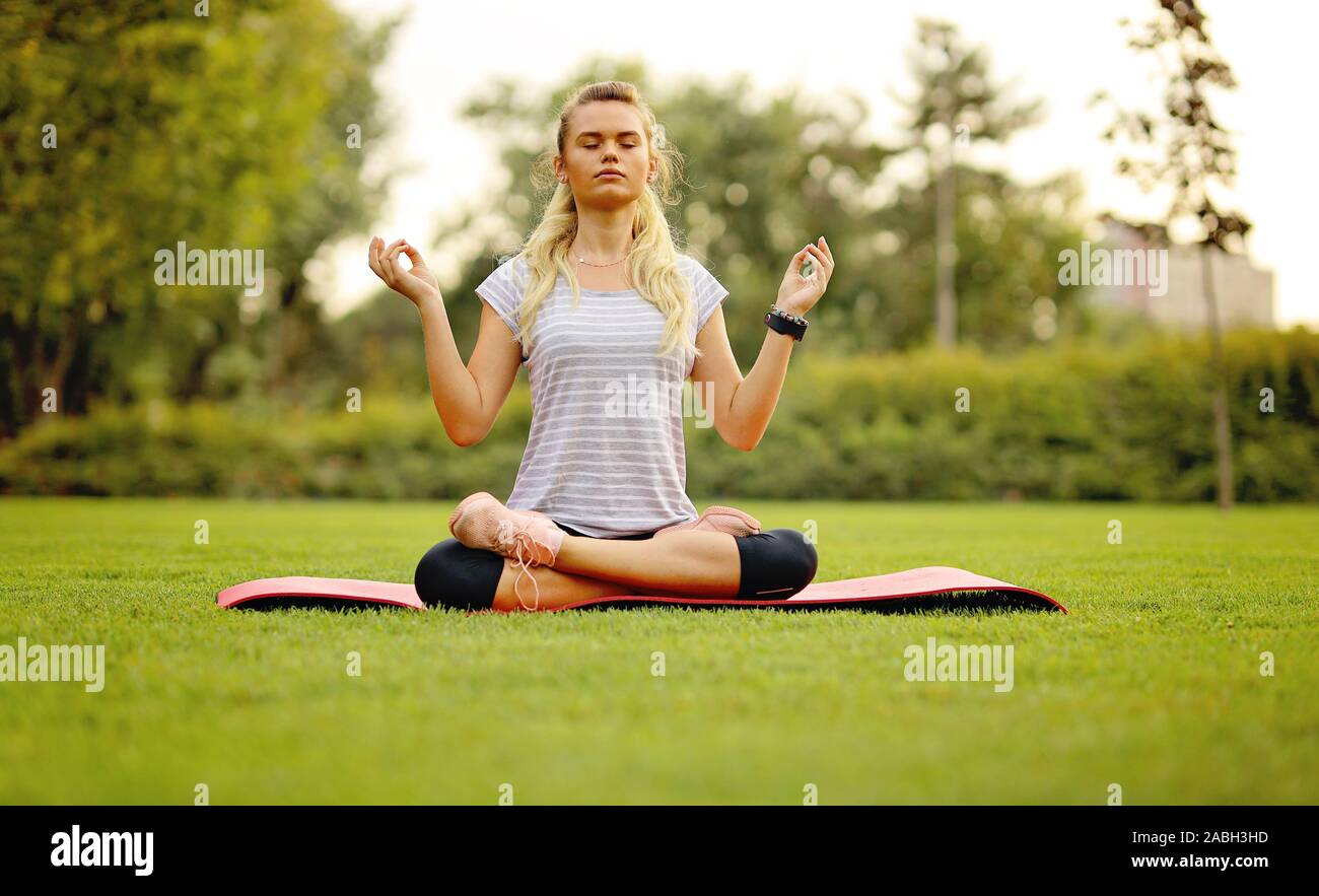 Young woman practicing yoga pose at the park on a beautiful green field ...