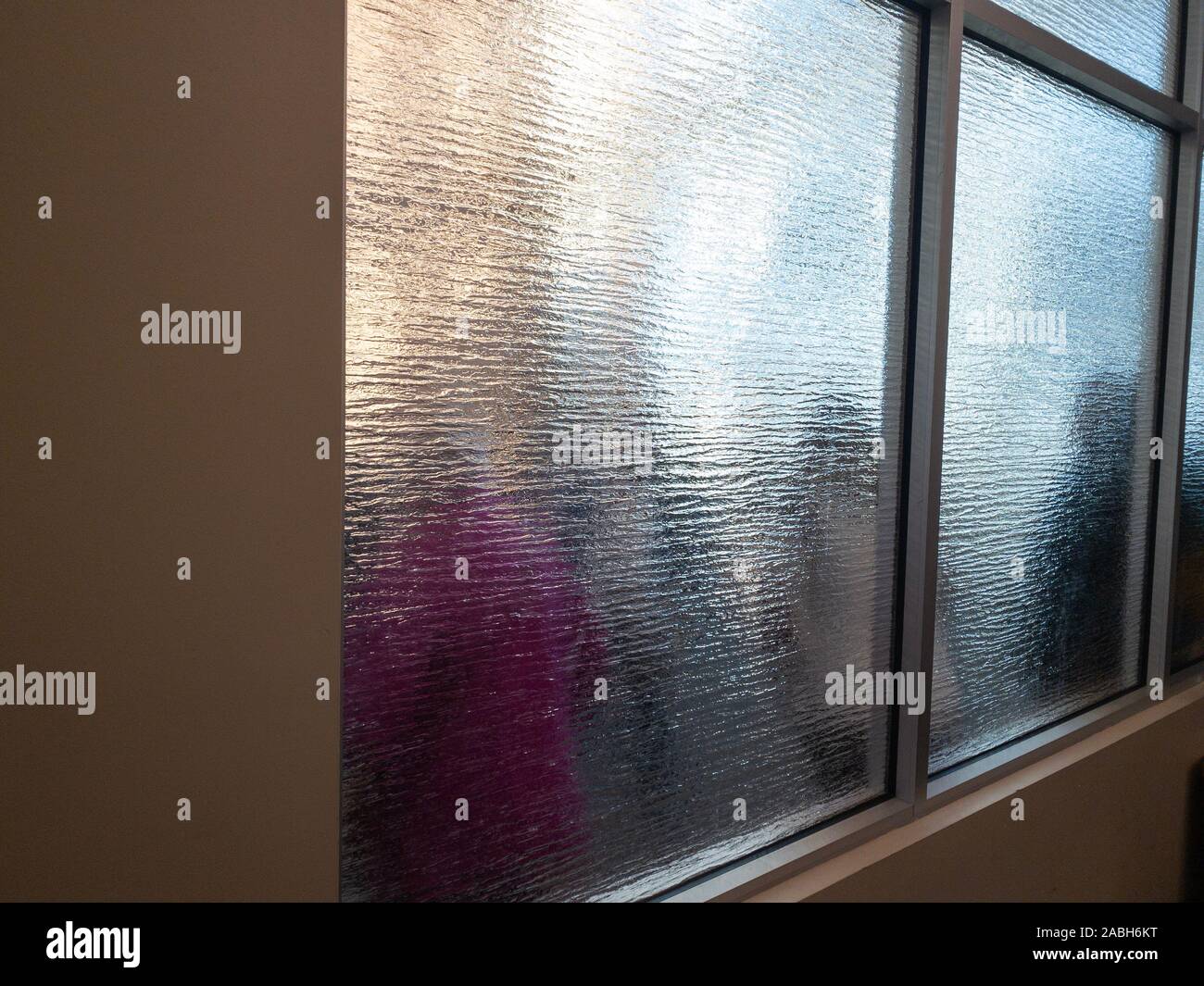 Blurred crowd of people standing or queuing behind textured frosted ...