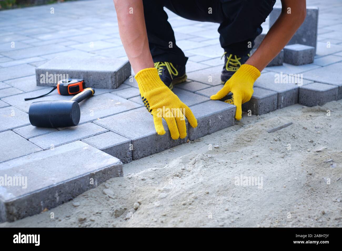 The master in yellow gloves lays paving stones in layers. Garden brick ...
