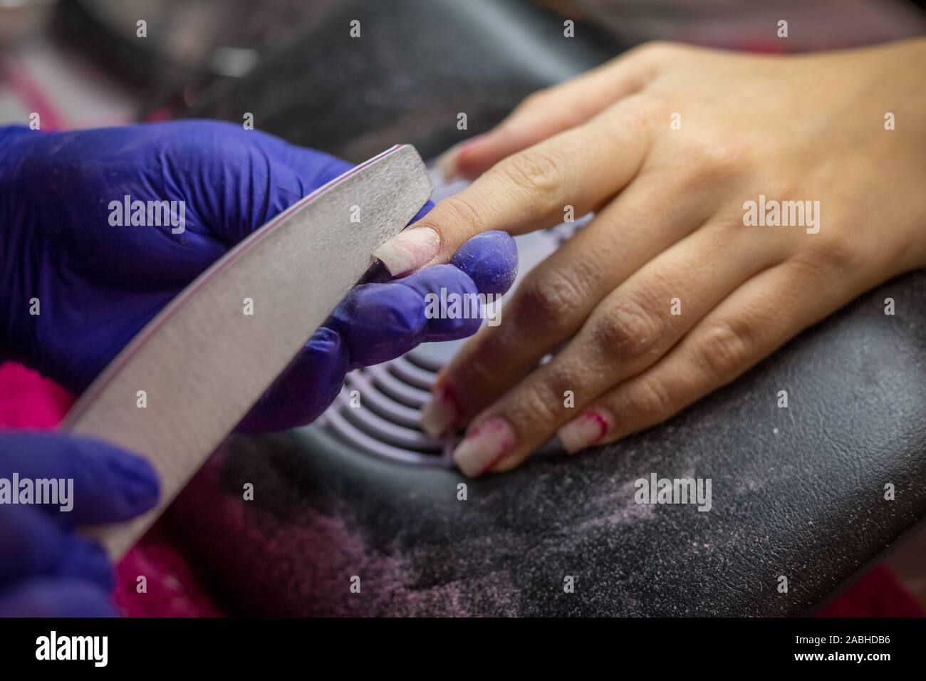 Manicurist with blue gloves rasping nails on women's hand in nail salon ...