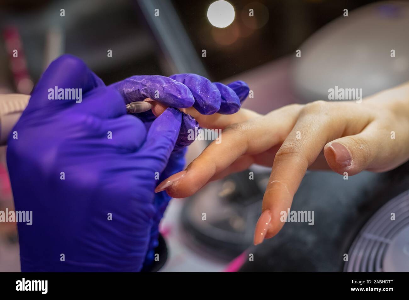 Manicurist with blue gloves rasping nails on women's hand in nail salon ...