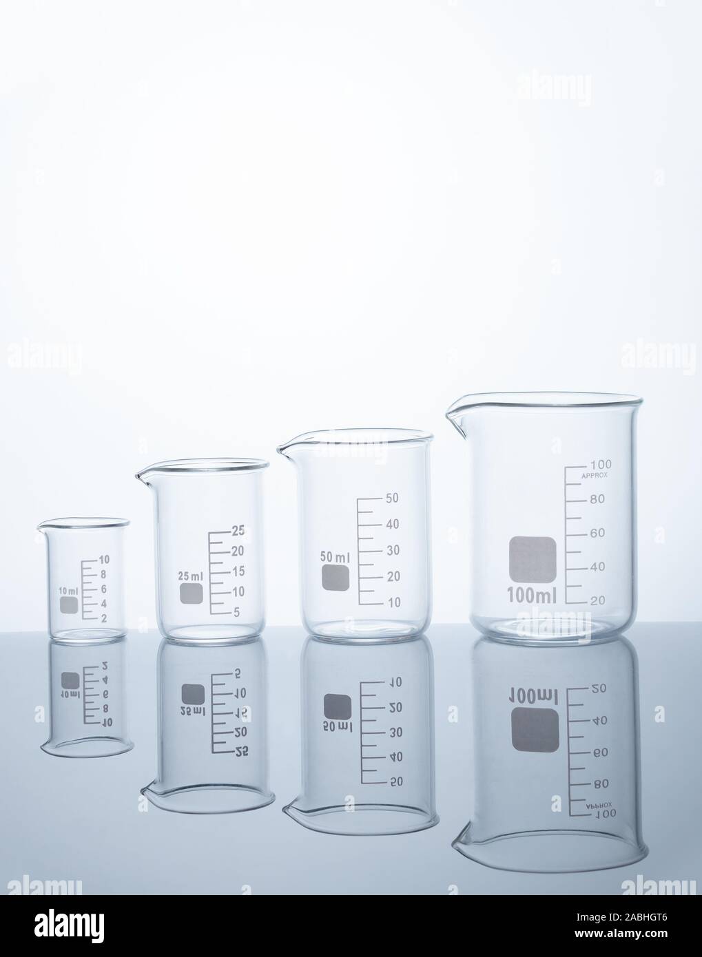 Four transparent measuring beakers sitting on a mirror blue surface ...