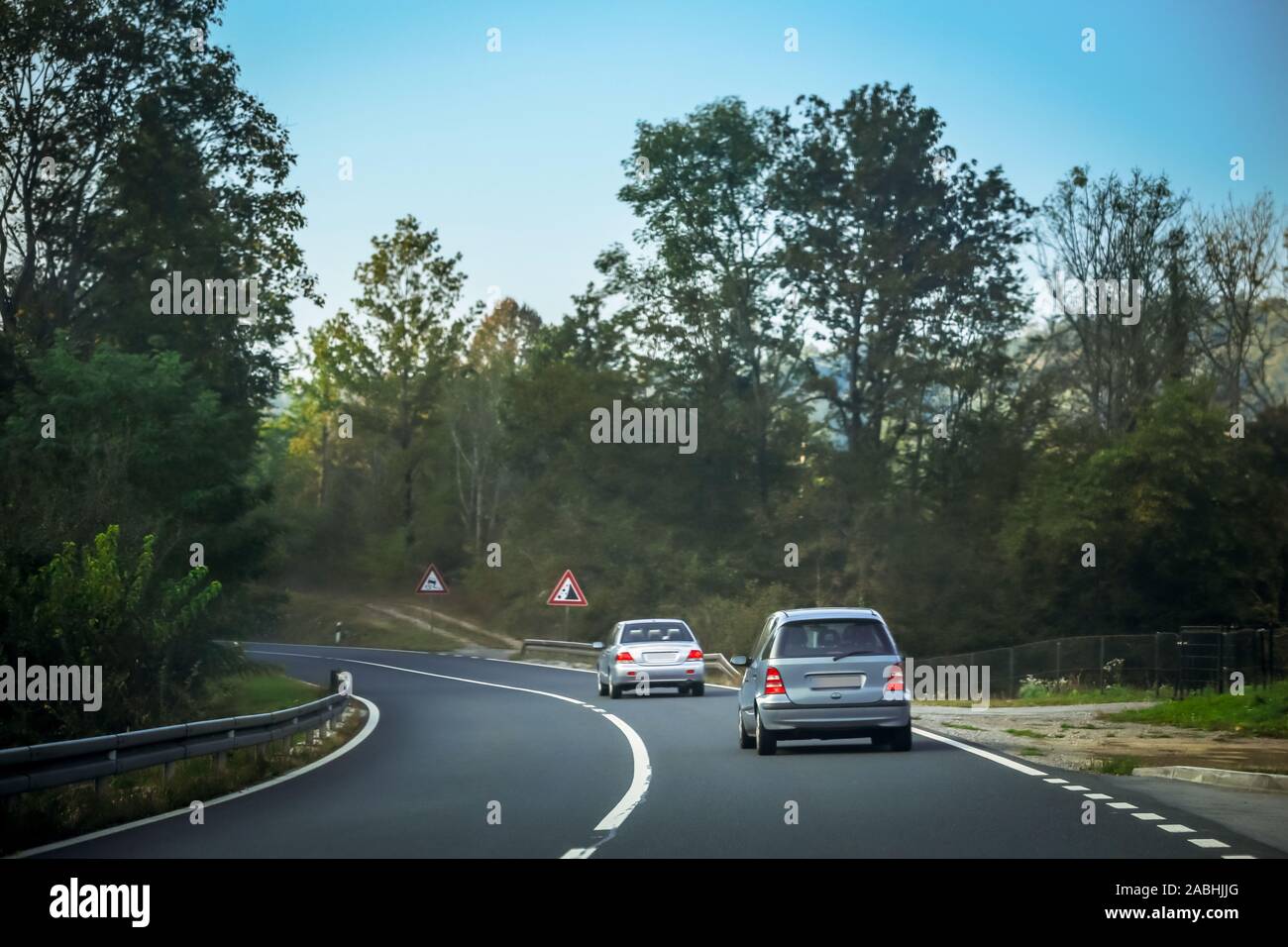 Rear view of two cars driving on the two way road thru the forest of ...