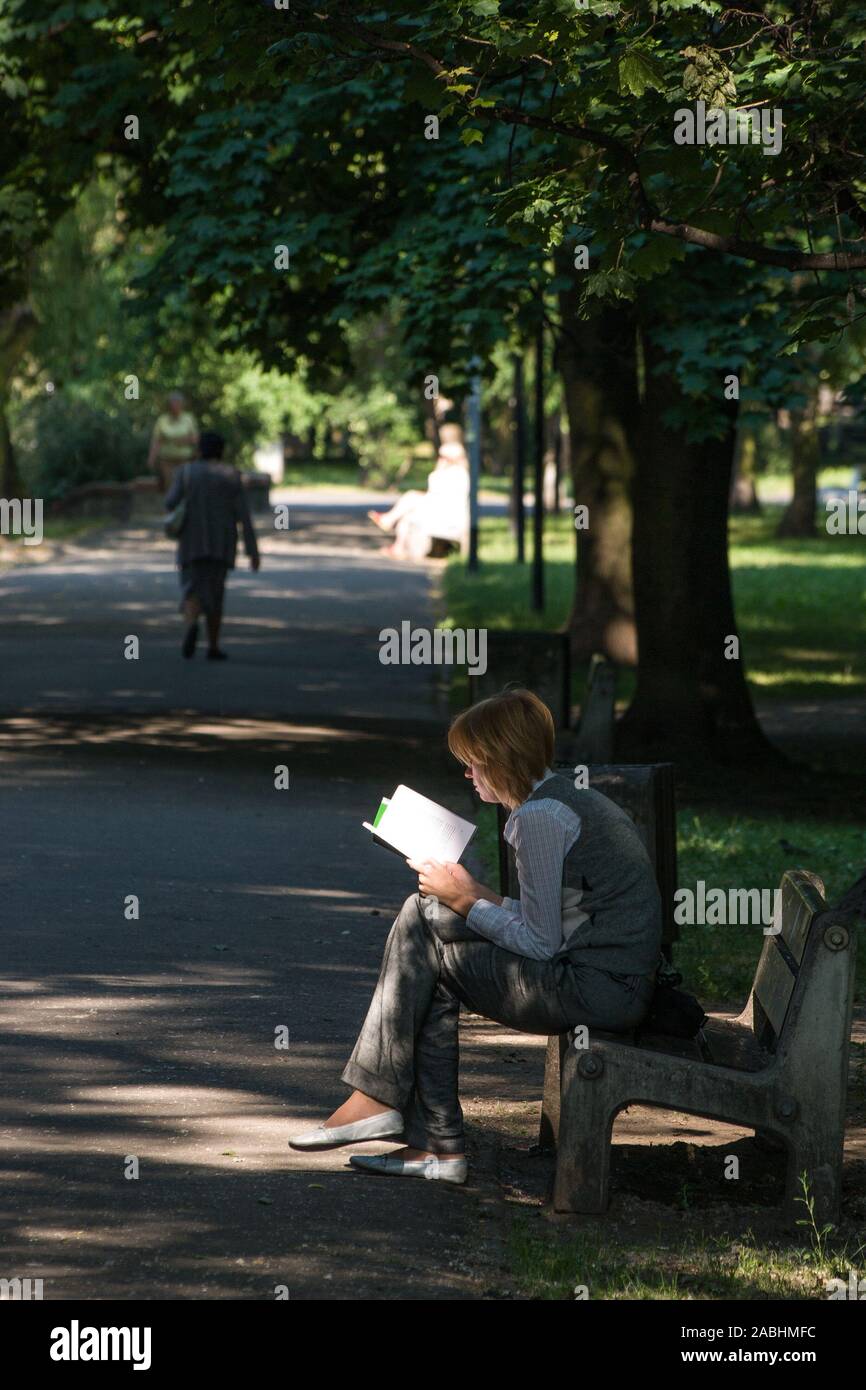 Young woman reading a book on a park bench Stock Photo - Alamy