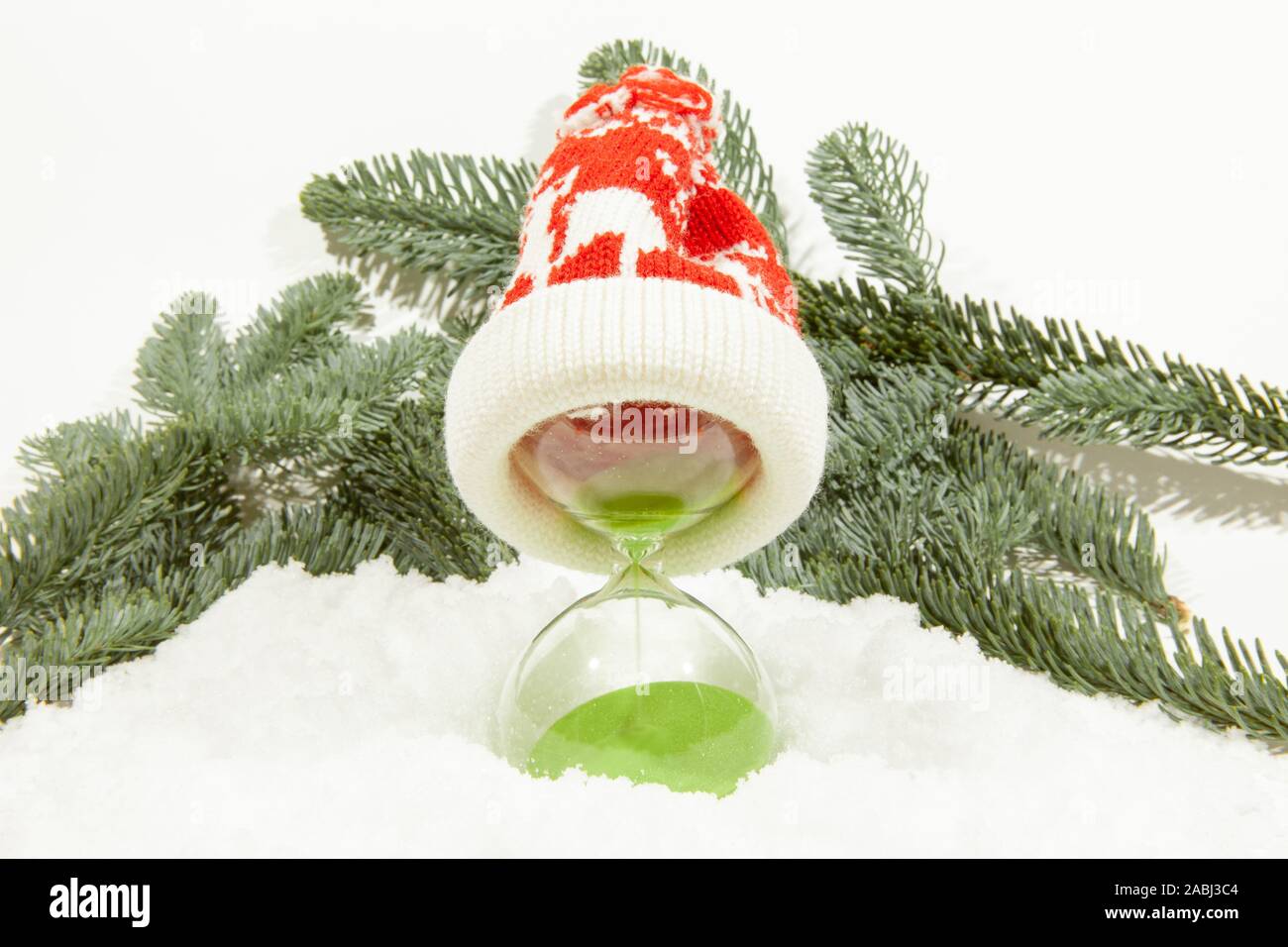 Hourglass in a Christmas hat, on the background of fir branches. The ...