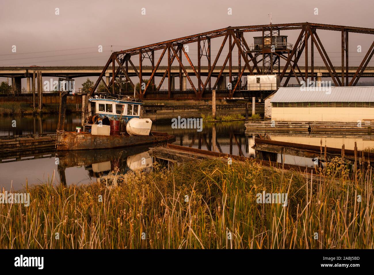 Old abandoned tug boat in industrial marina with train trestle in ...