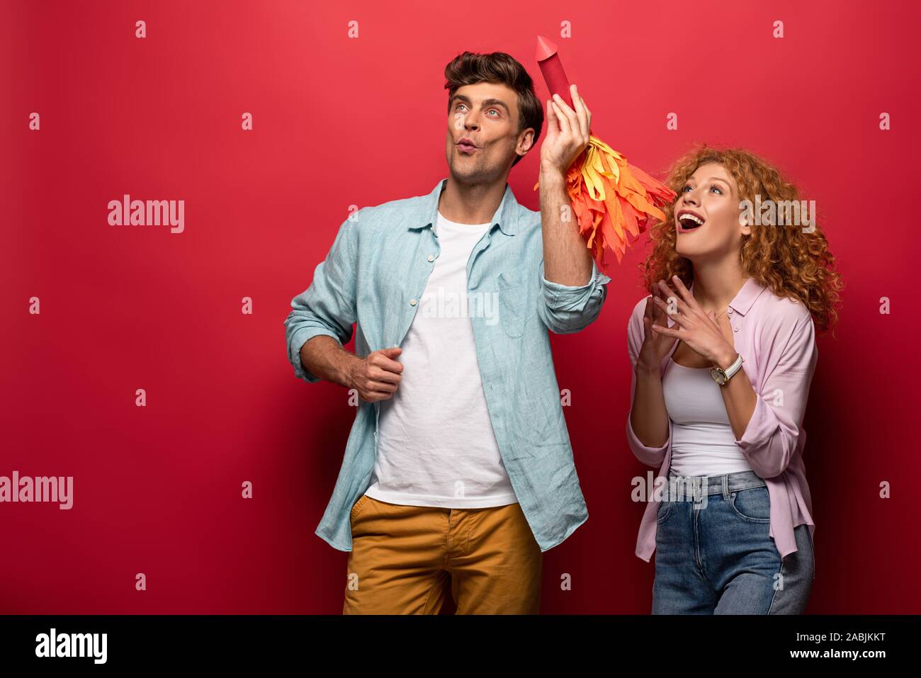 excited beautiful couple throwing little rocket, on red Stock Photo - Alamy