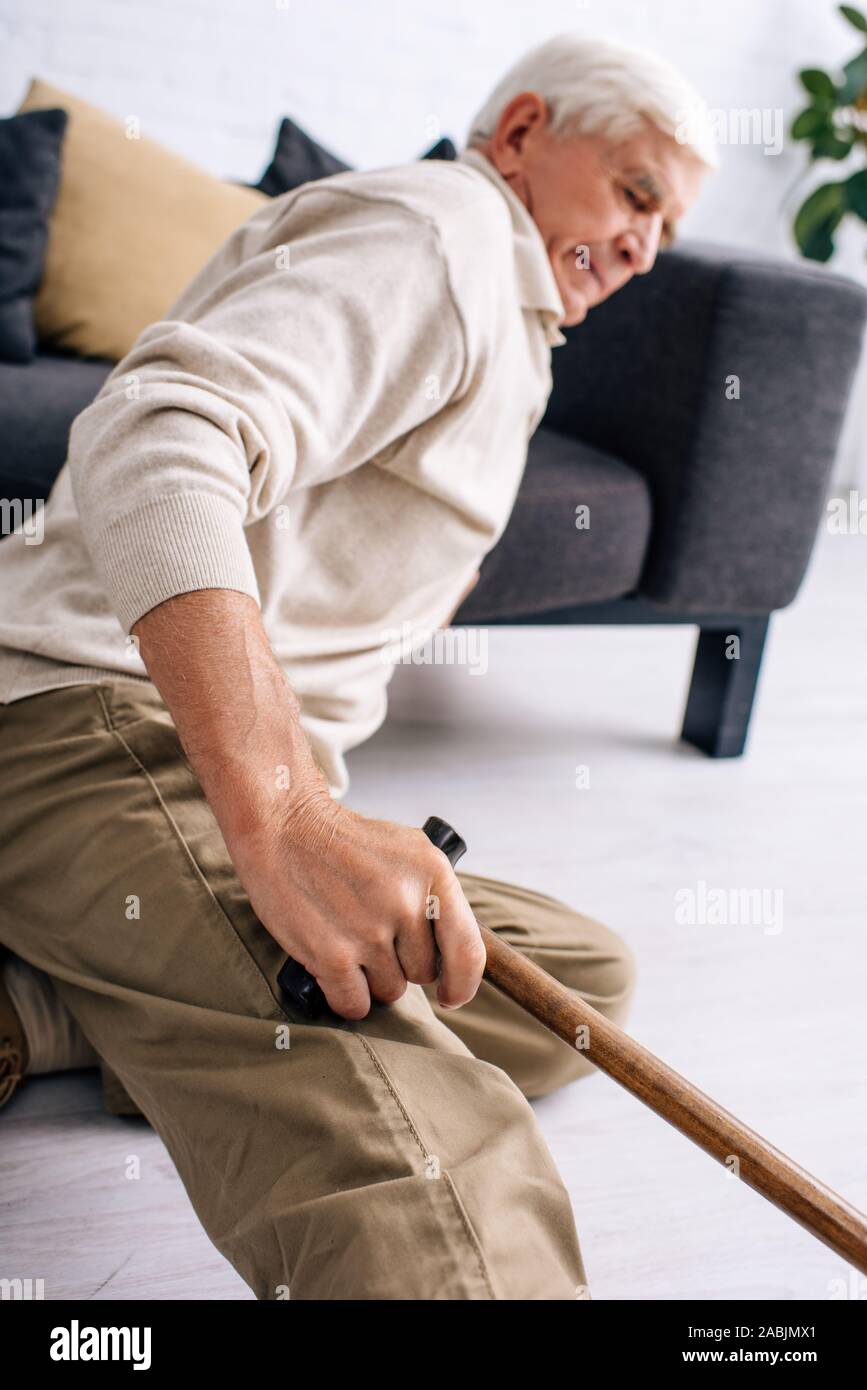 selective focus of senior man holding wooden cane and feeling pain in ...