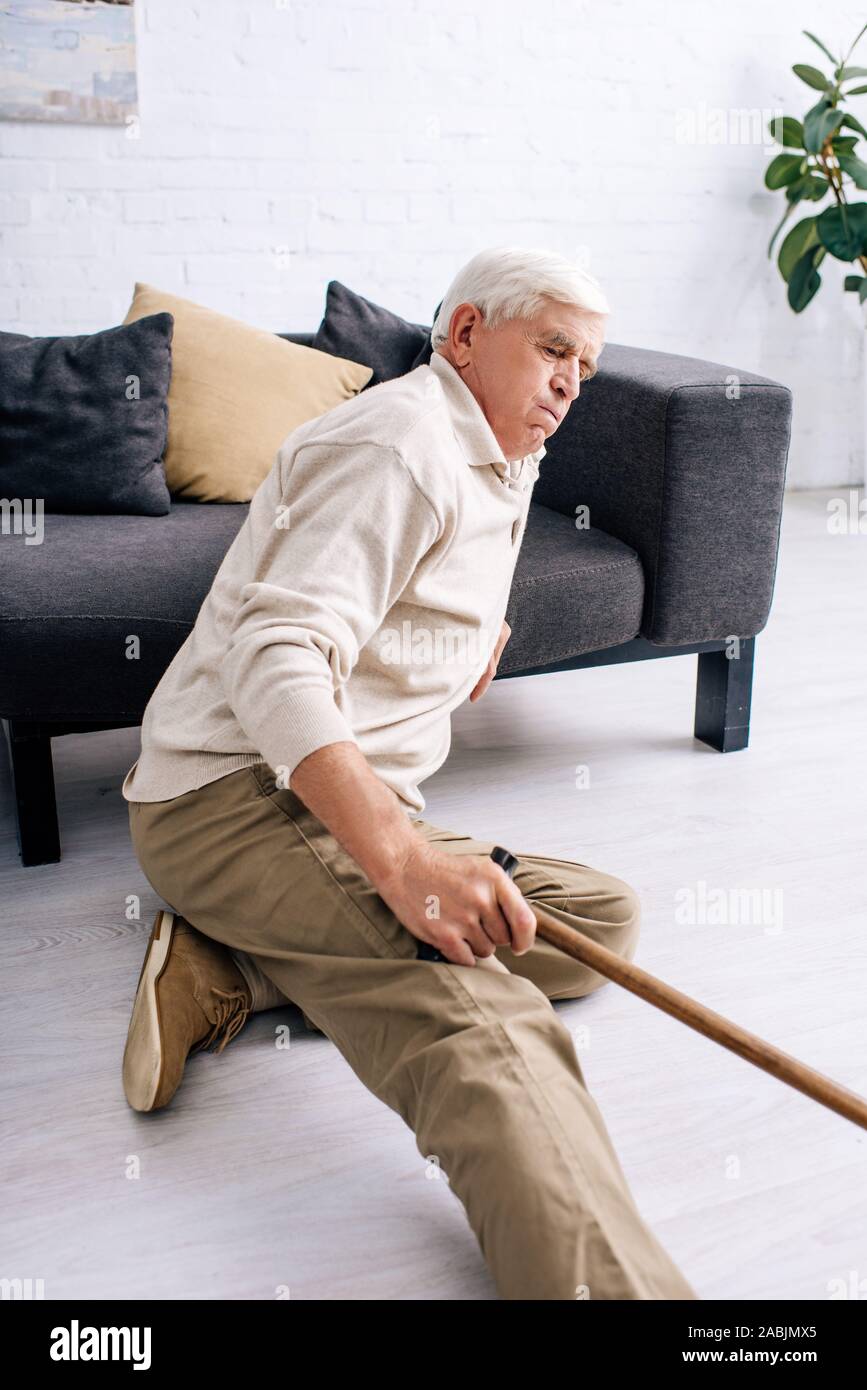 senior man holding wooden cane and feeling pain in apartment Stock ...