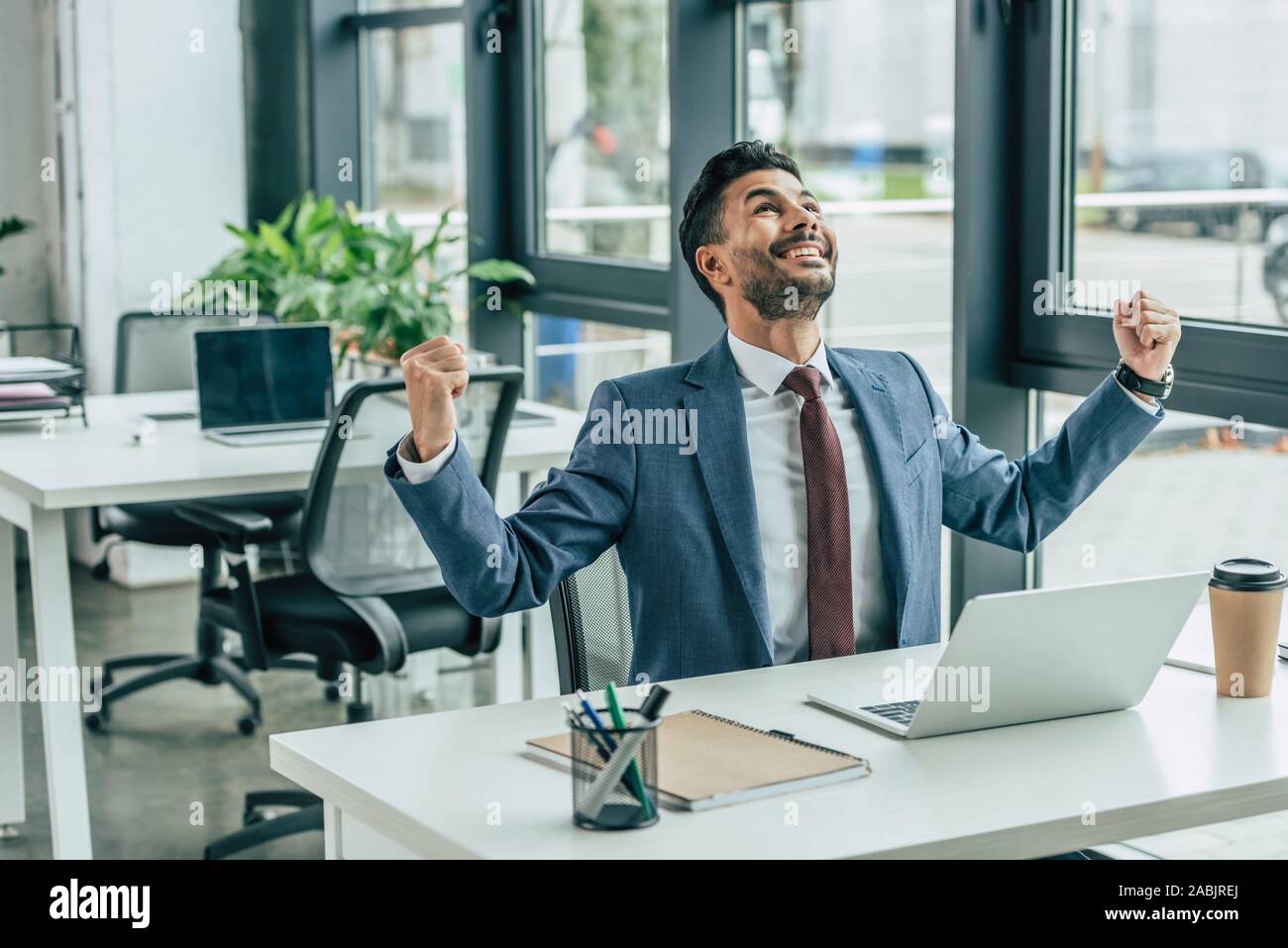 happy businessman looking up and showing winner gesture while sitting ...