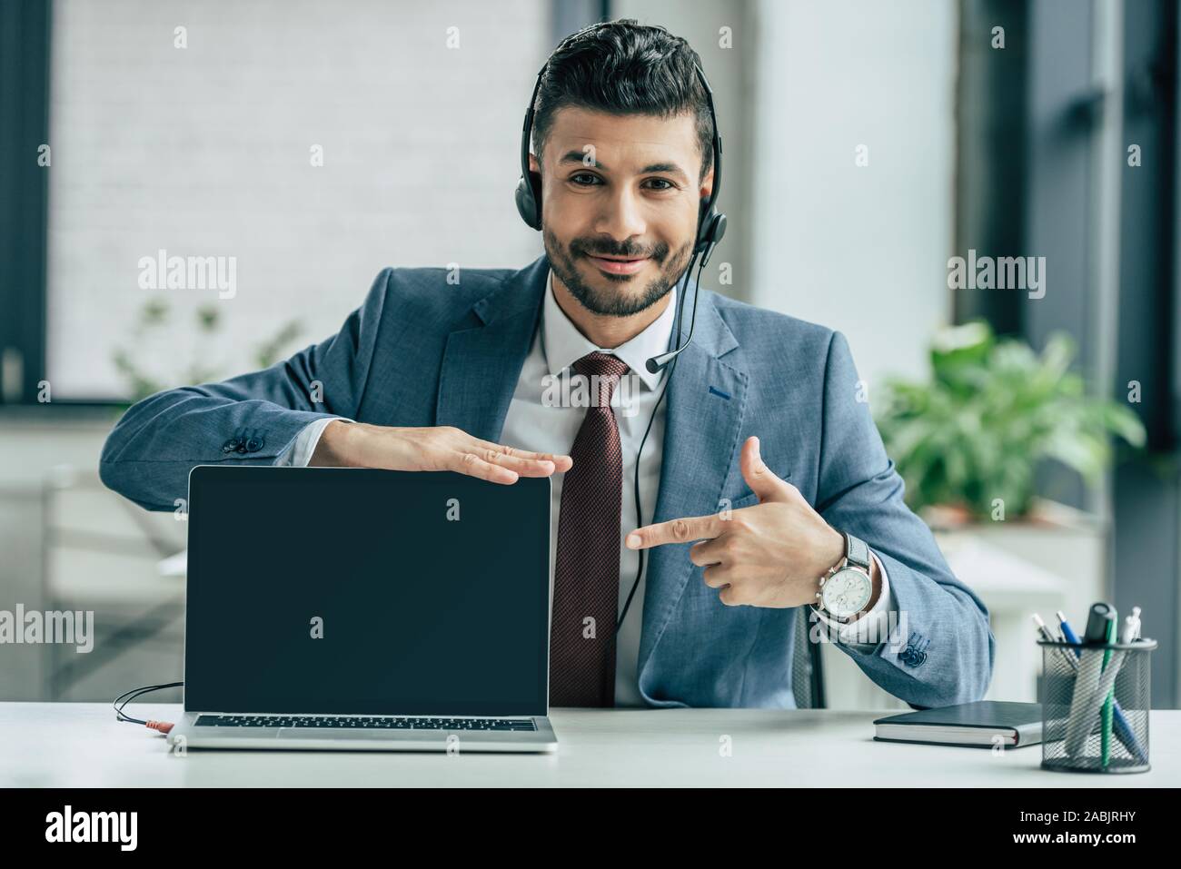 cheerful call center operator pointing with finger at laptop with blank ...