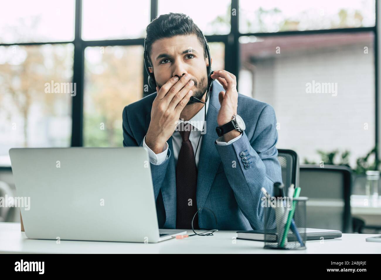shocked call center operator in headset looking away and covering mouth ...