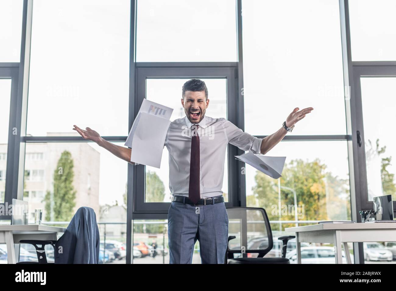 angry businessman throwing papers and yelling while standing in modern ...
