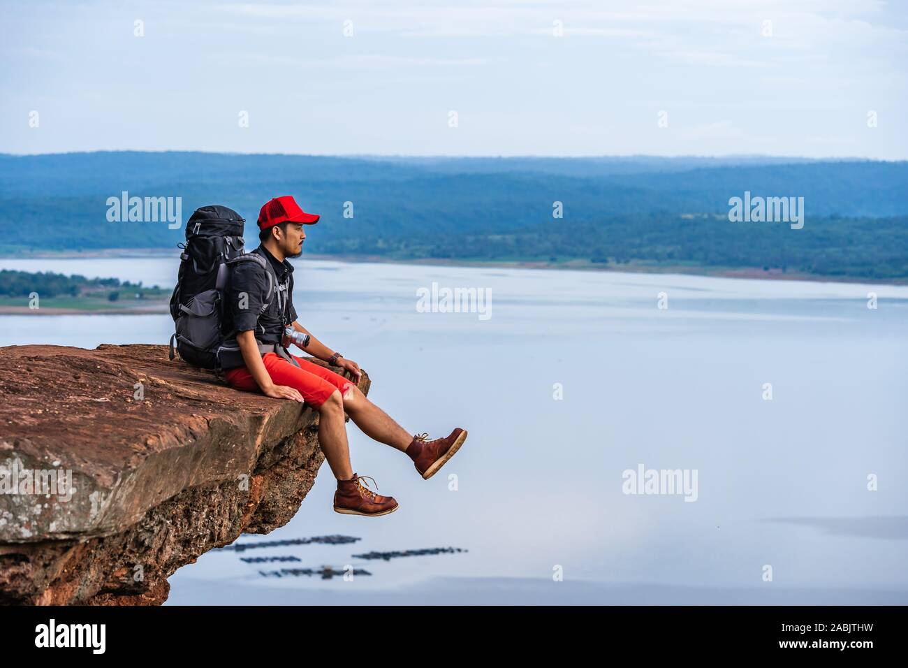 man traveler with backpack sitting on the edge of cliff, on a top of ...