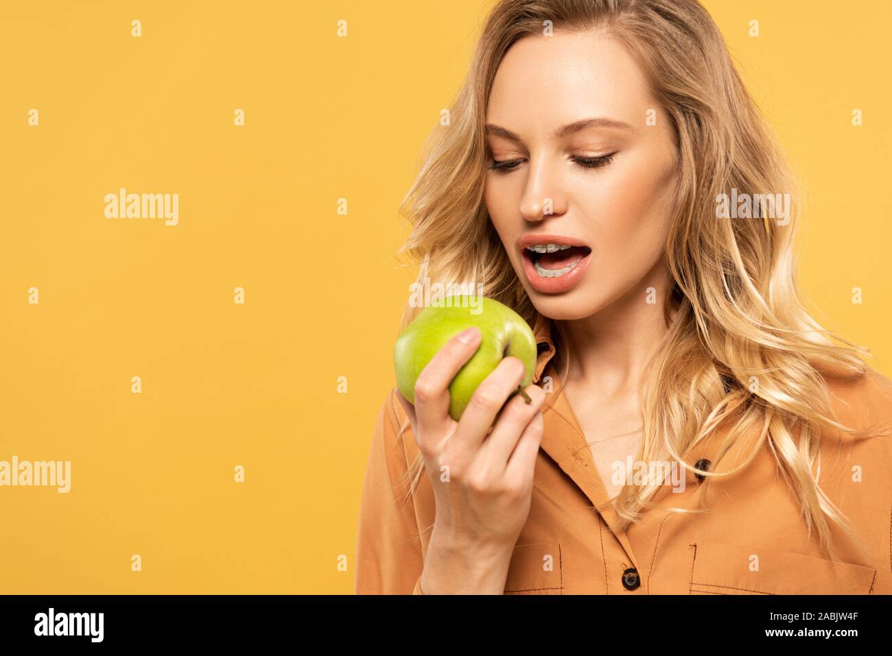 Young woman with dental braces biting green apple isolated on yellow ...