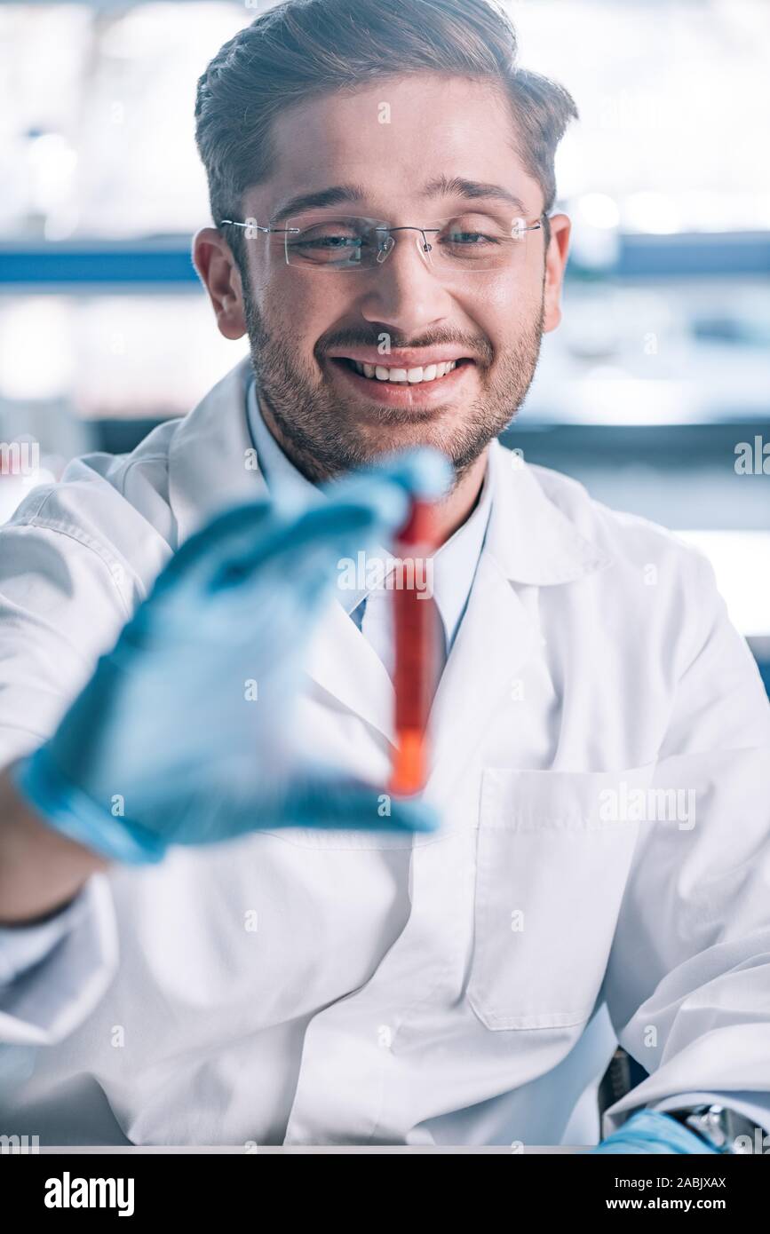 selective focus of happy immunologist holding test tube with red liquid ...