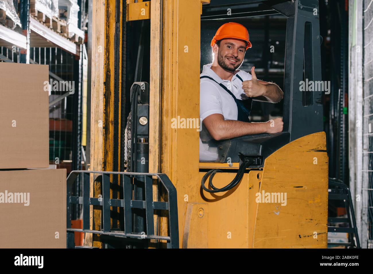 smiling warehouse worker showing thumb up and looking at camera while ...