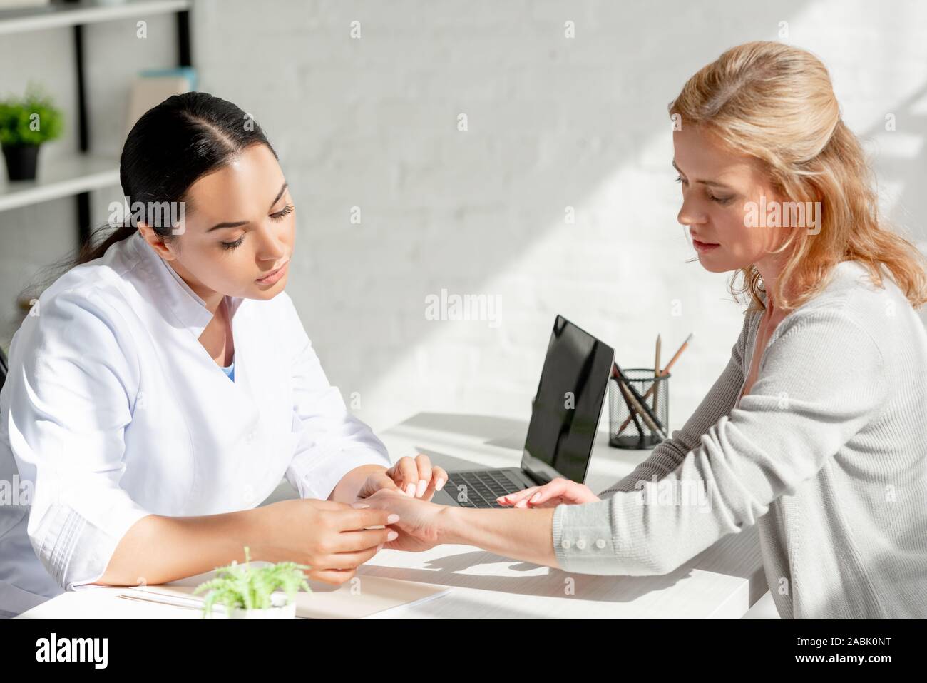 dermatologist sitting at table examining skin of patient in clinic ...