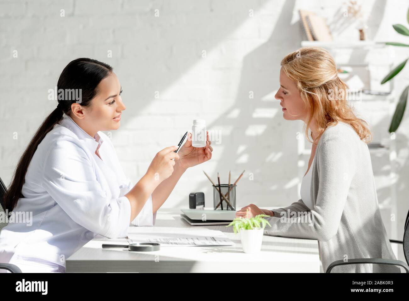 side view of dermatologist showing bottle with pills to patient in ...
