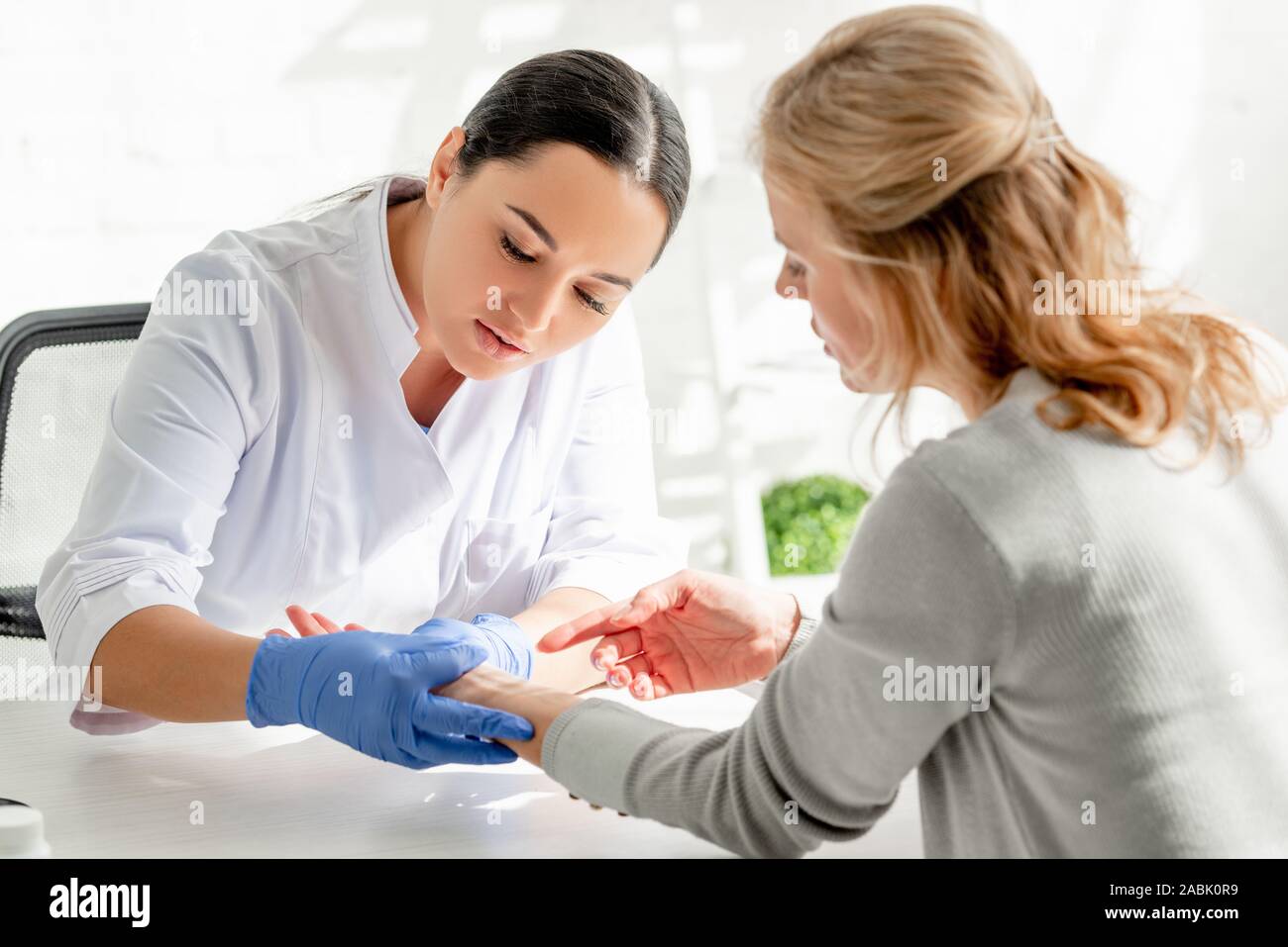 attractive dermatologist in white coat examining skin of patient in ...