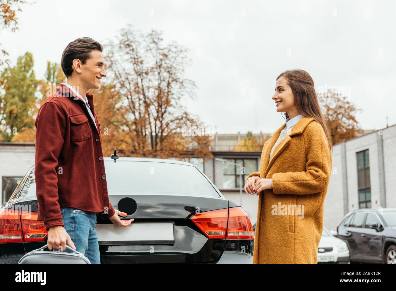 Taxi driver helping woman with baggage beside car trunk Stock Photo - Alamy