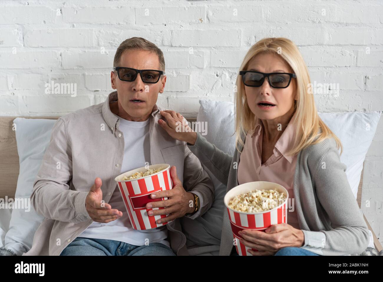 Shocked couple in 3d glasses and buckets with popcorn on bed Stock Photo - Alamy