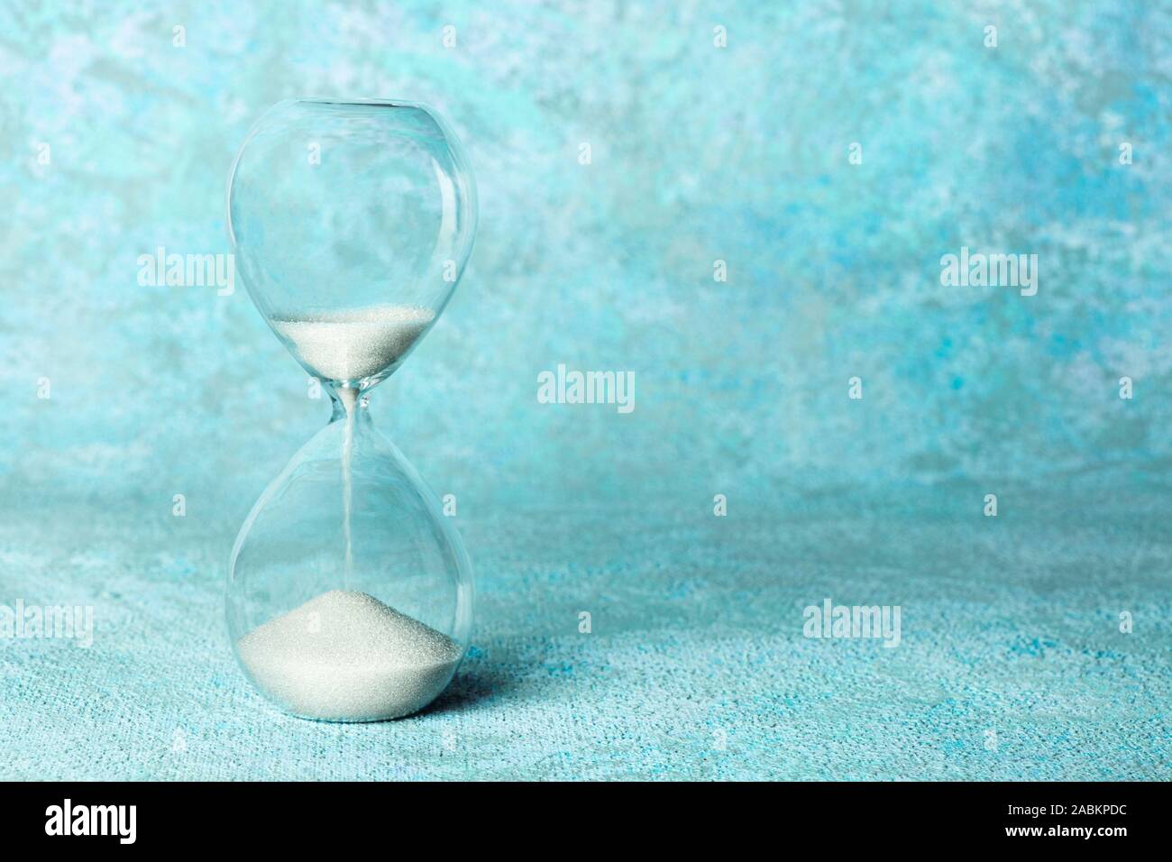 An hourglass on a teal blue background with a place for text. Time ...