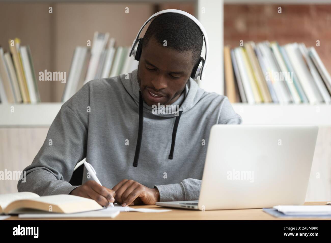 Focused black student wearing bluetooth earphones, busy with study ...