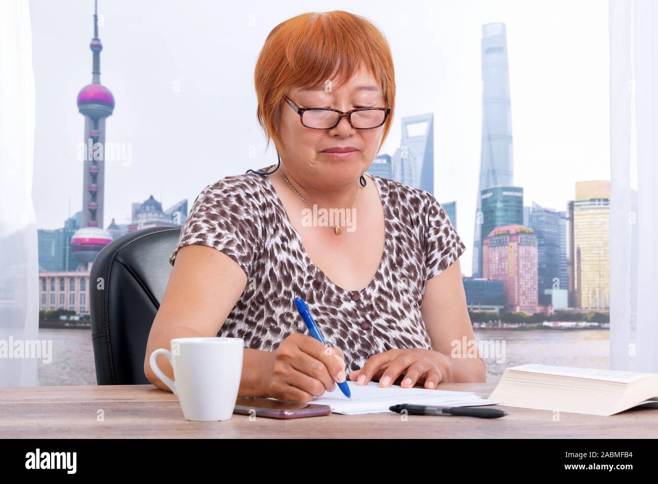 Asian female professor in the office with glasses looking and writing ...