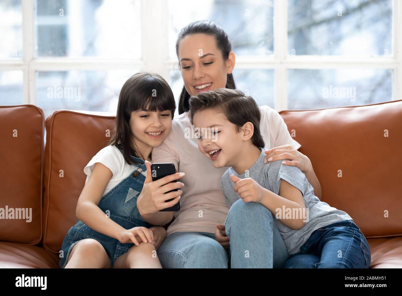 Smiling kids have fun watching video on cell with mom Stock Photo - Alamy