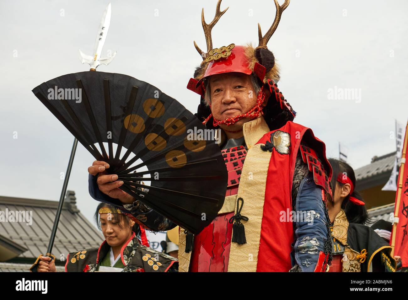 Japanese man in yoroi armor holding a black fan walks in a parade of ...