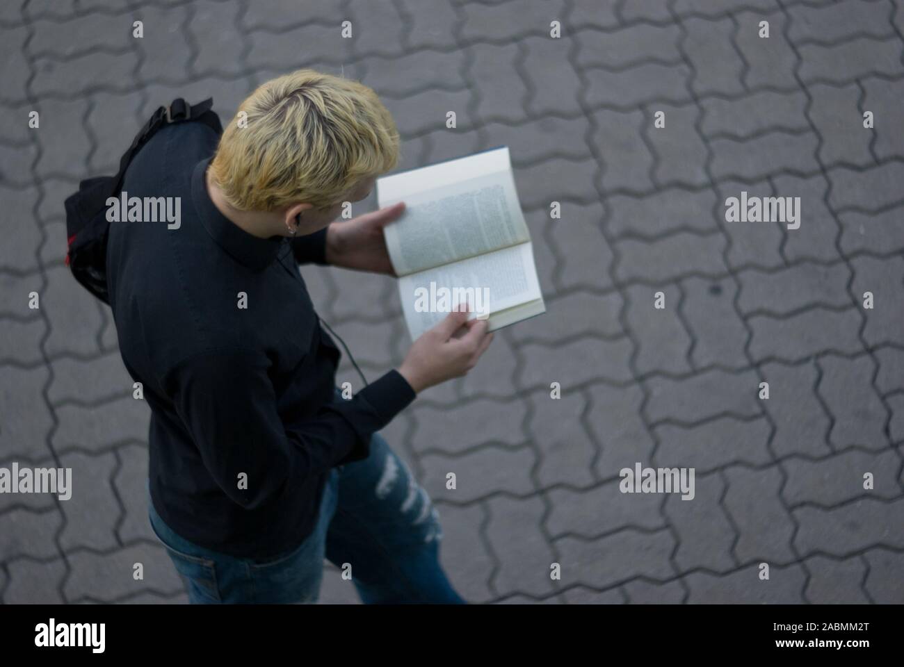 View from above of a young man reading a book walking down the sidewalk ...